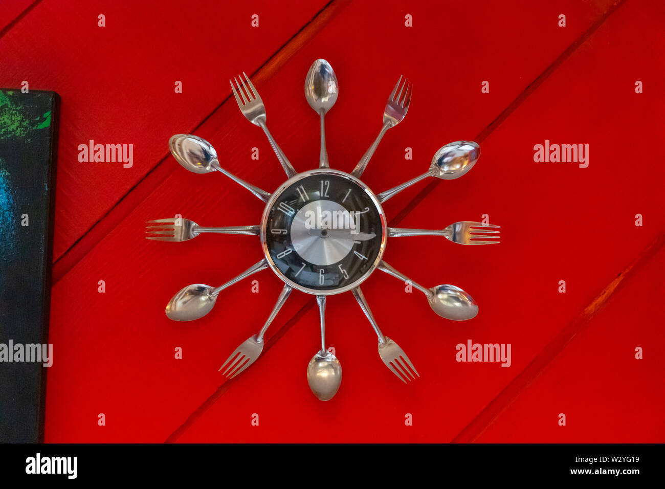 Clock with spoon and fork dials on red wall Stock Photo - Alamy