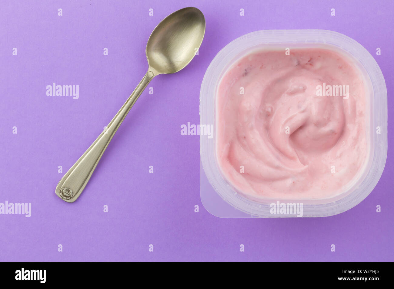 Yogurt cup with pink strawberry yogurt and small silver spoon isolated ...
