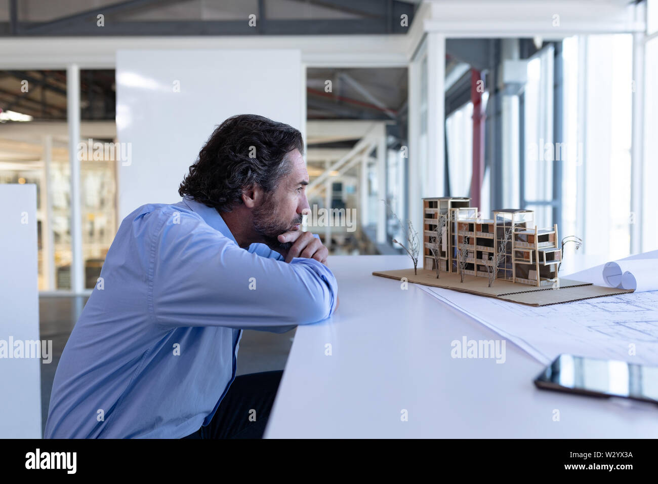 Male architect looking at architectural model at table in a modern ...
