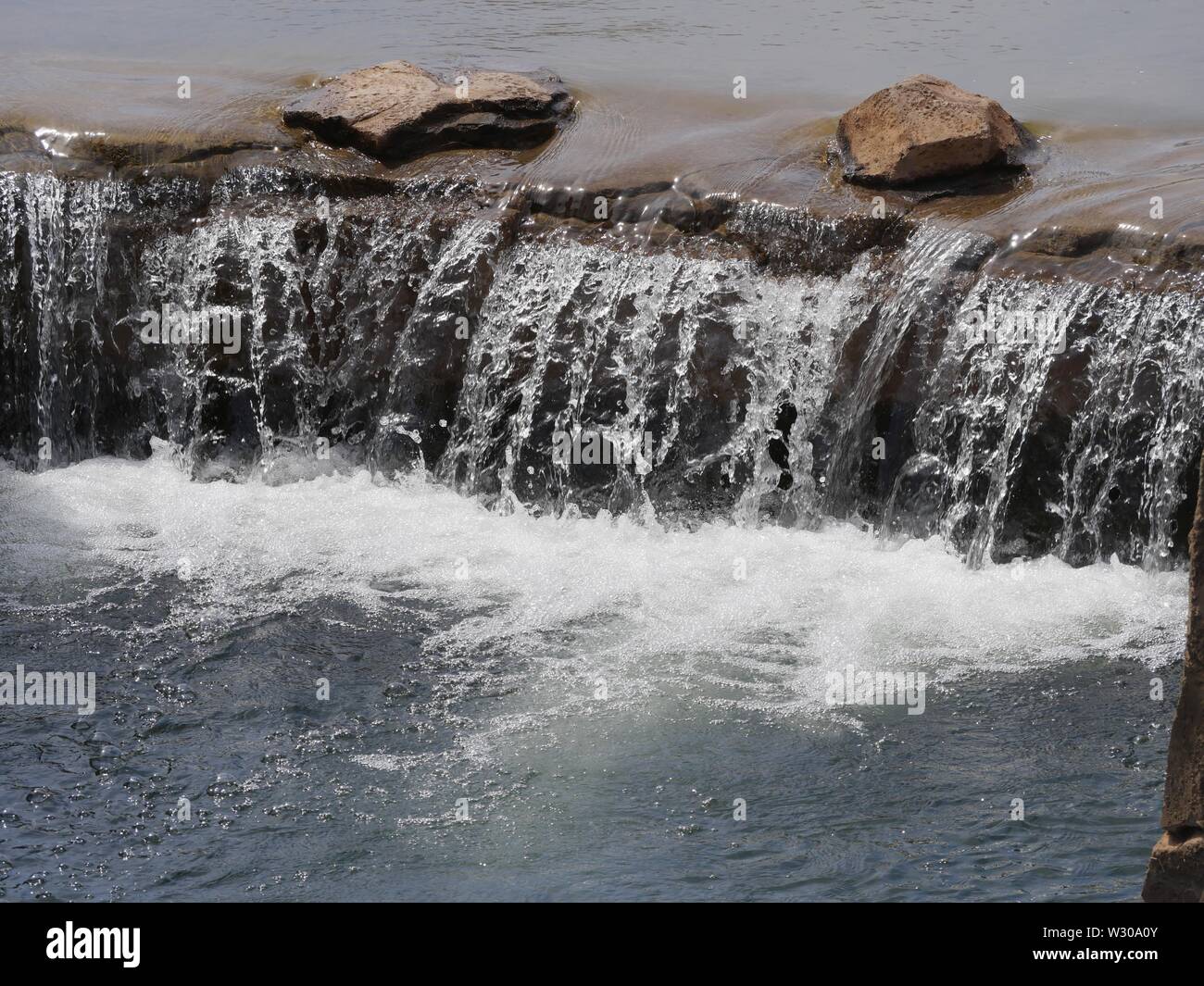 Water cascading and making ripples from a small waterfall in a river ...