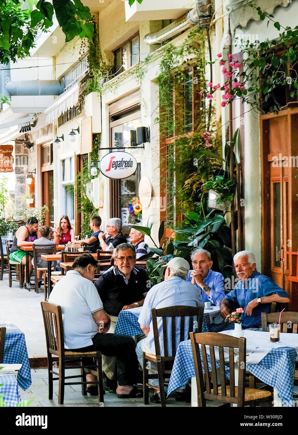 Greek men sitting in outdoor cafes in village square of Mochos, Crete ...