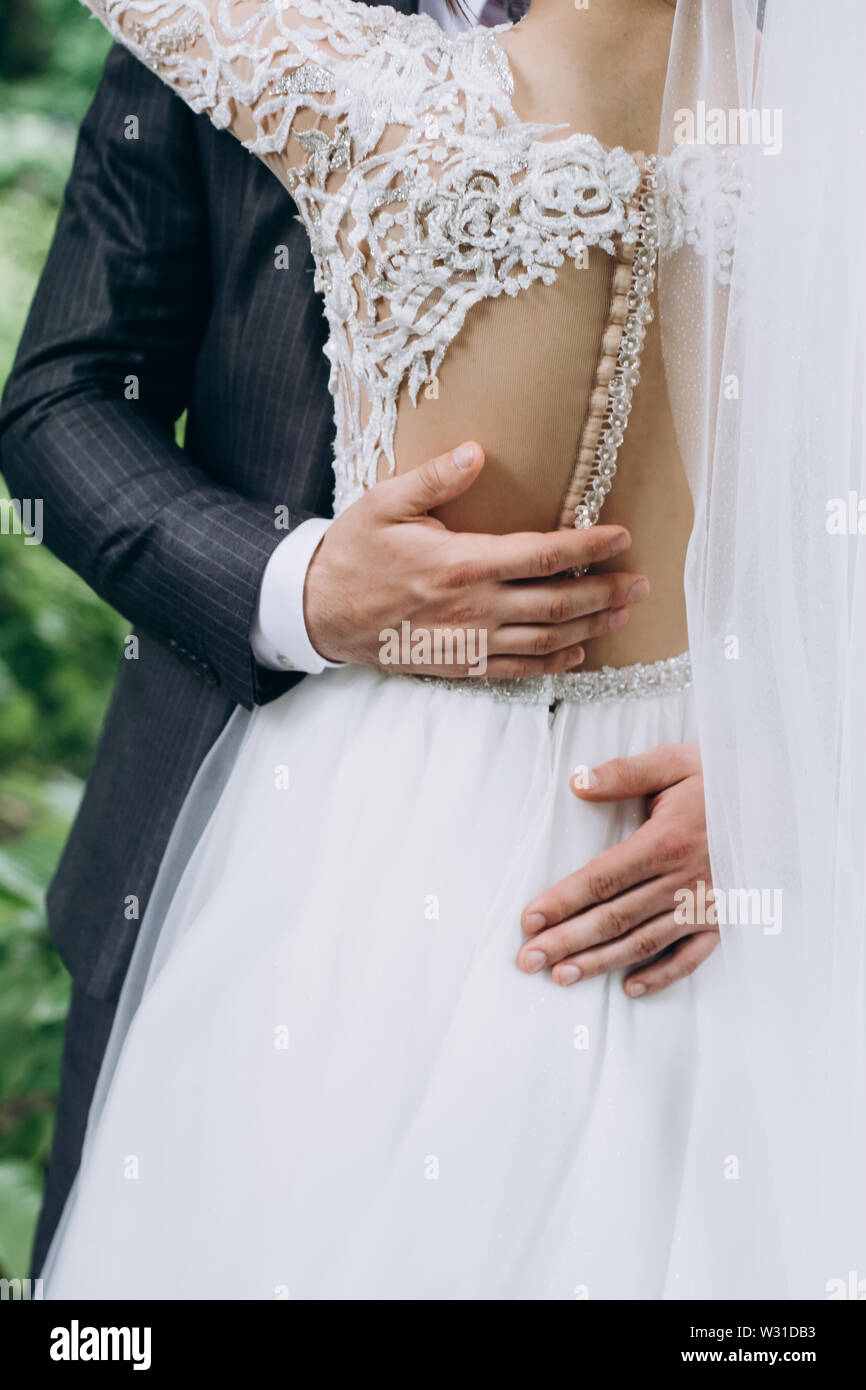 Rear view of bride in a white dress and groom hugs, blurred green ...