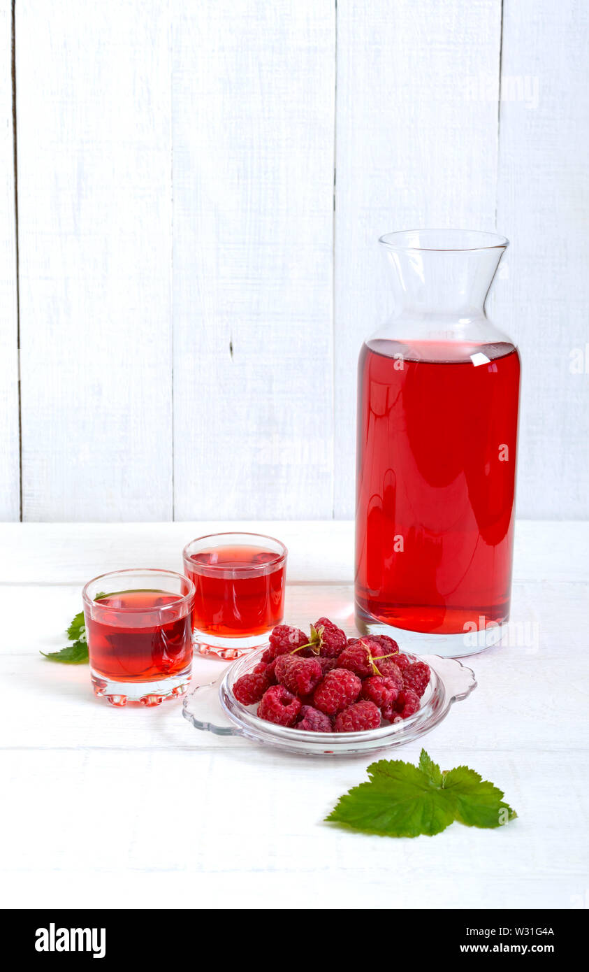 Raspberry liqueur in glass and fresh berries on a white background ...