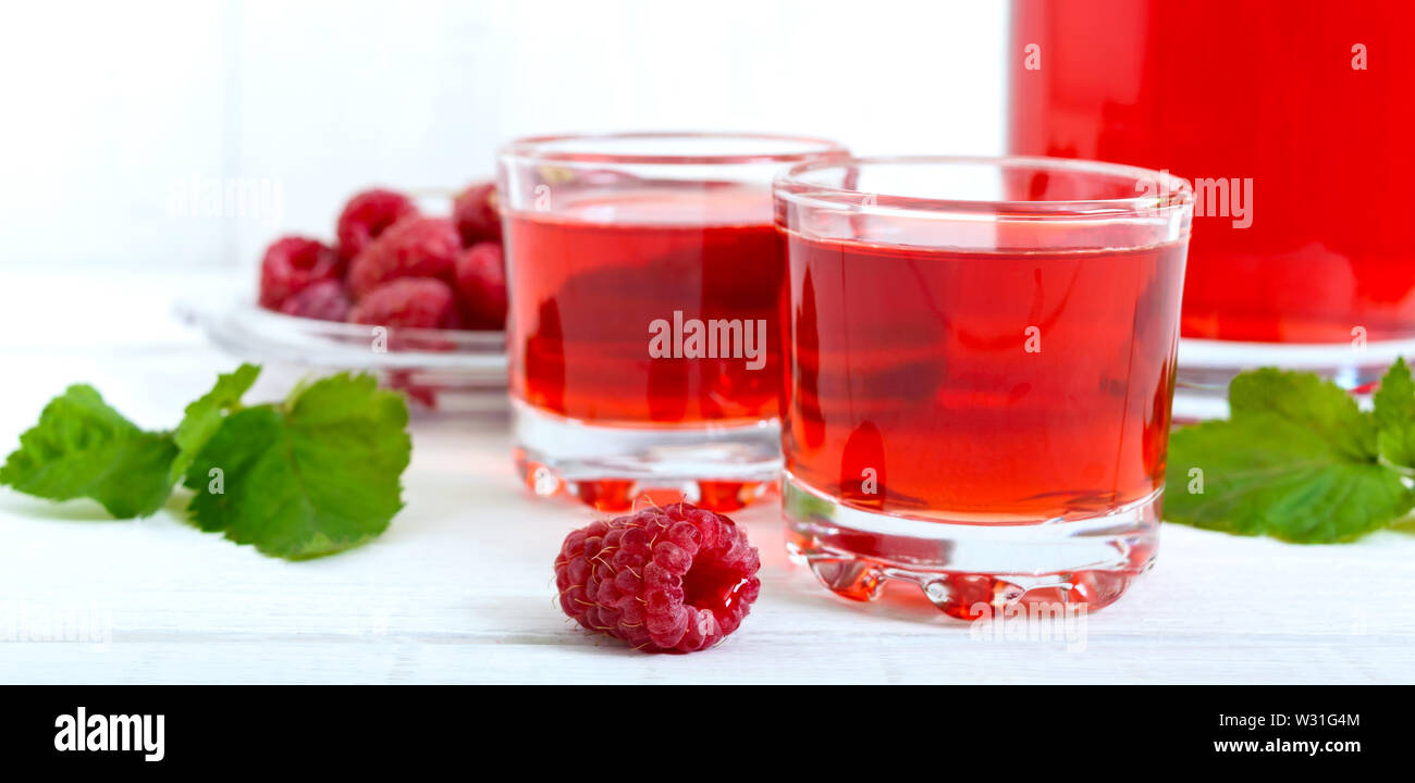 Raspberry liqueur in glass and fresh berries on a white background ...
