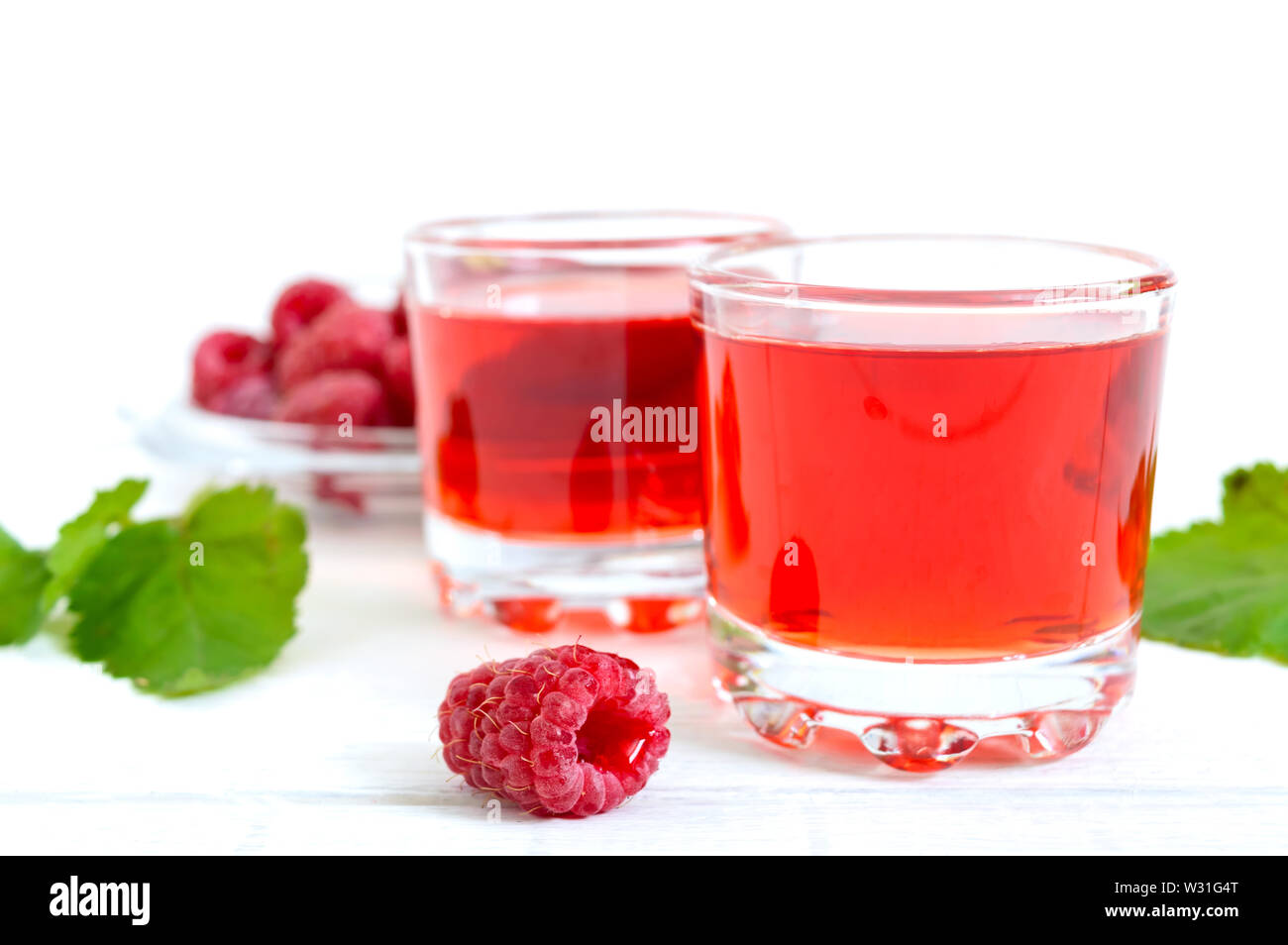 Raspberry liqueur in glass and fresh berries on a white background ...