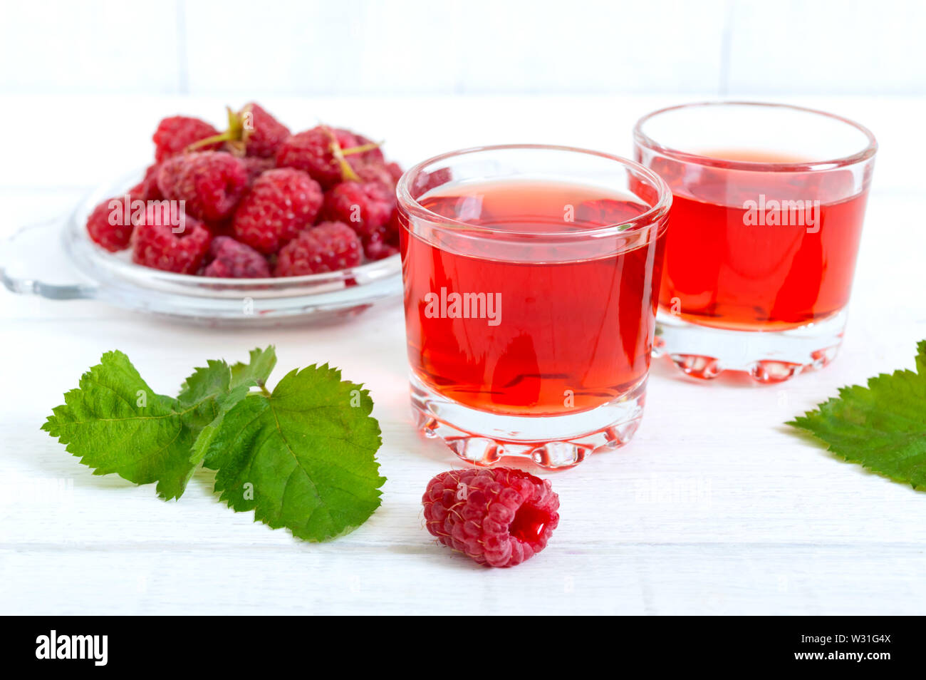 Raspberry liqueur in glass and fresh berries on a white background ...