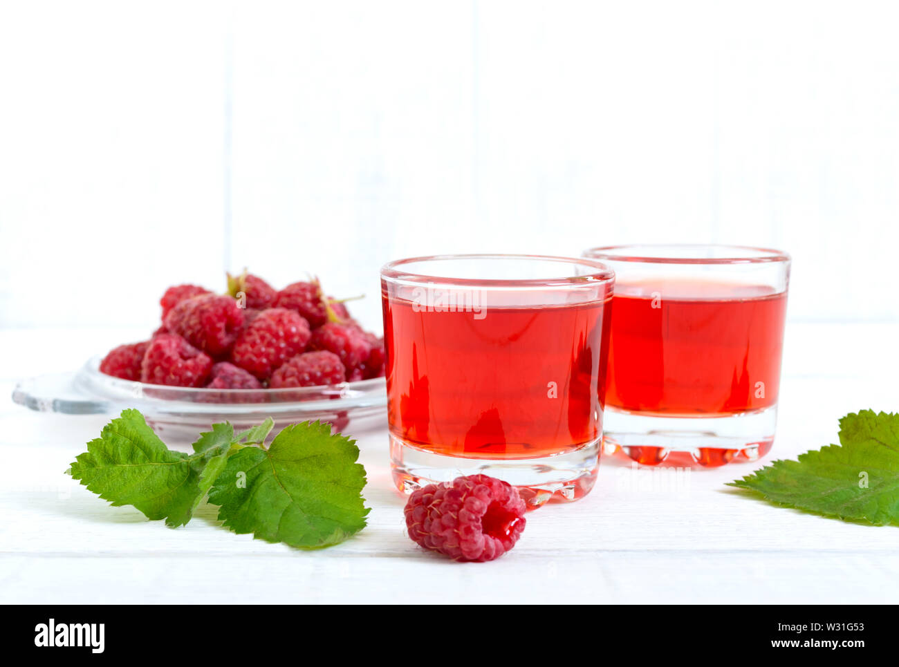 Raspberry liqueur in glass and fresh berries on a white background ...