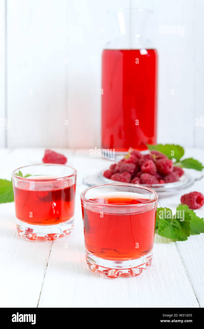 Raspberry liqueur in glass and fresh berries on a white background ...