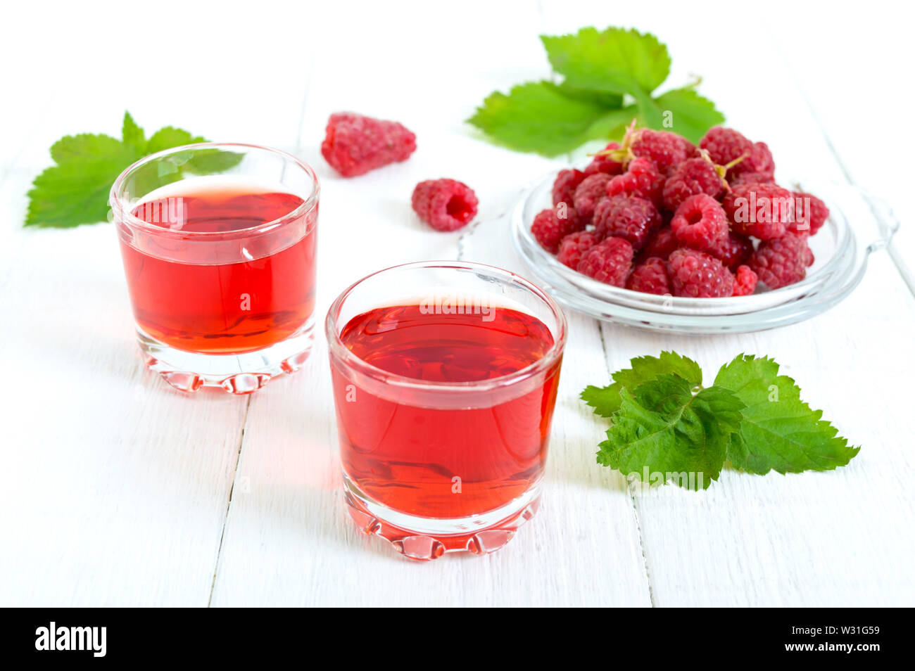 Raspberry liqueur in glass and fresh berries on a white background ...
