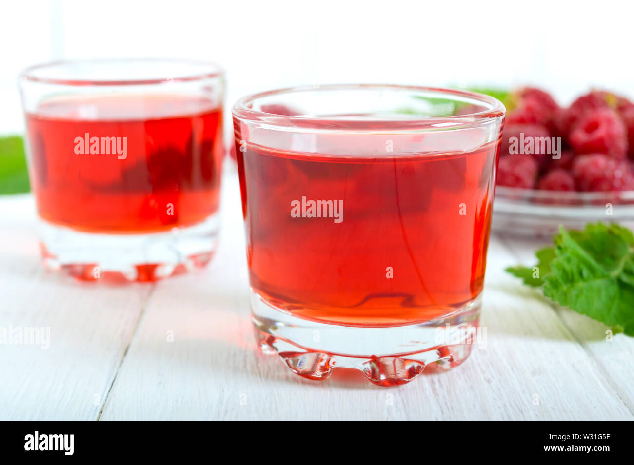 Raspberry liqueur in glass and fresh berries on a white background ...