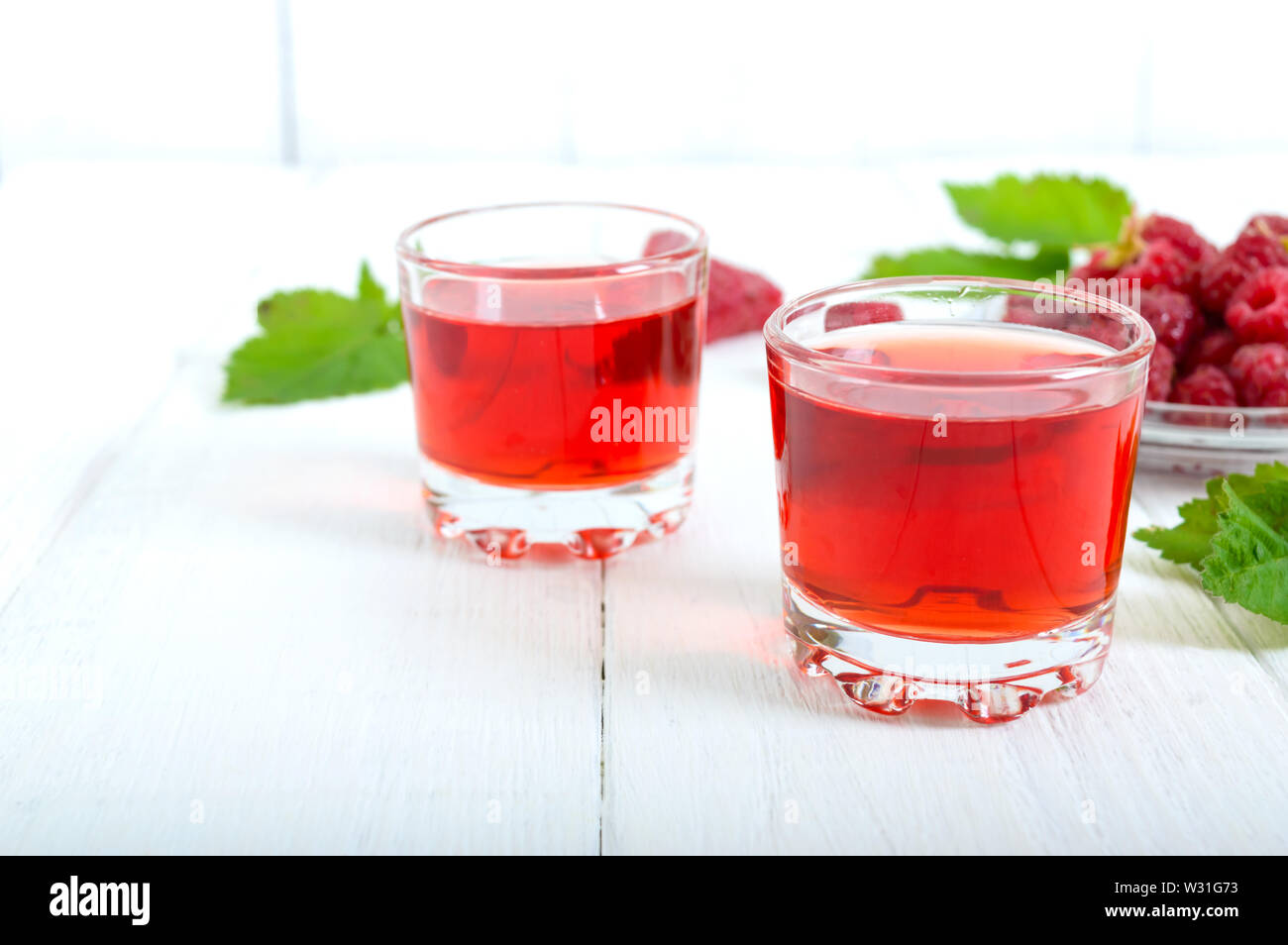 Raspberry liqueur in glass and fresh berries on a white background ...