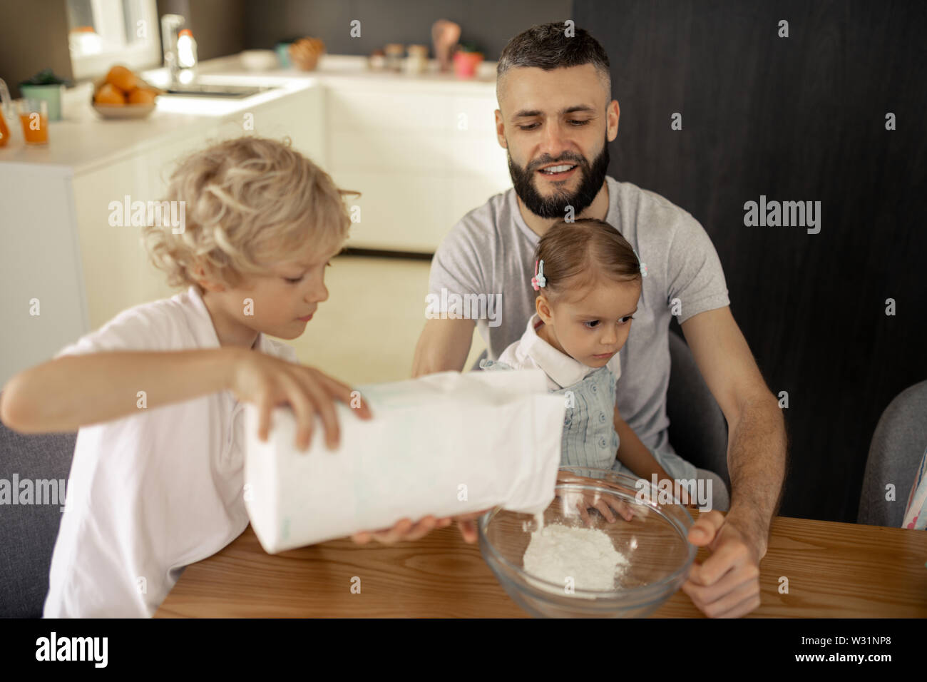 Young helper. Nice blonde boy holding a pack with flour while helping ...