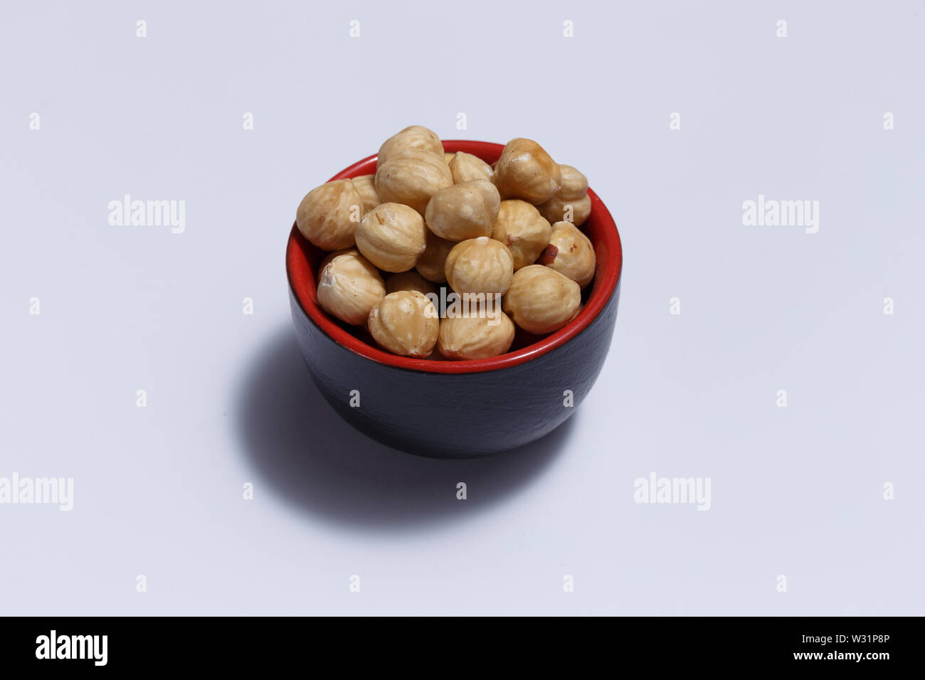 Front view of hazelnuts inside a red bowl isolated on white background ...