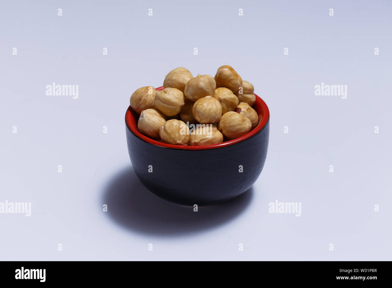 Front view of hazelnuts inside a red bowl isolated on white background ...