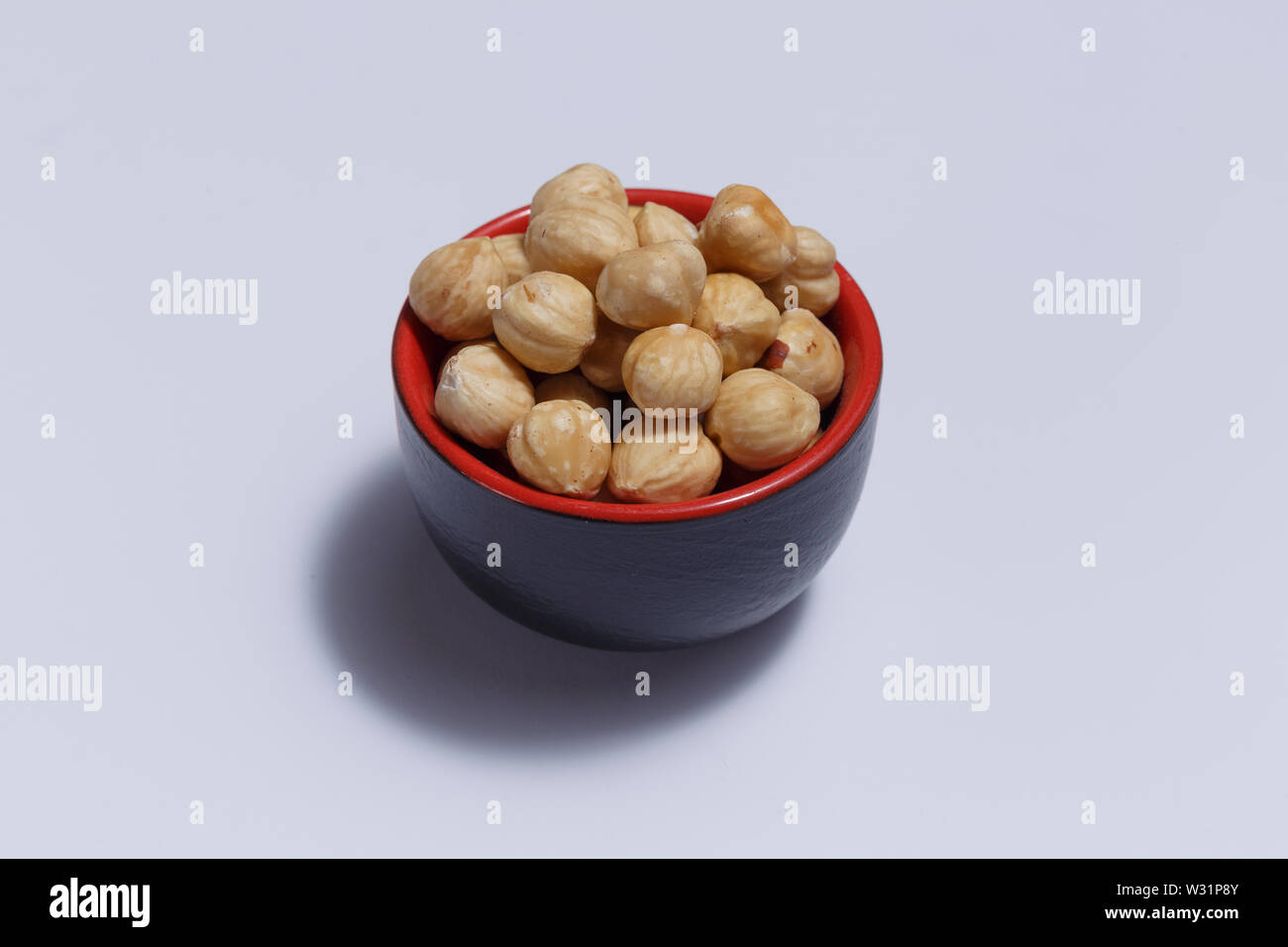 Front view of hazelnuts inside a red bowl isolated on white background ...