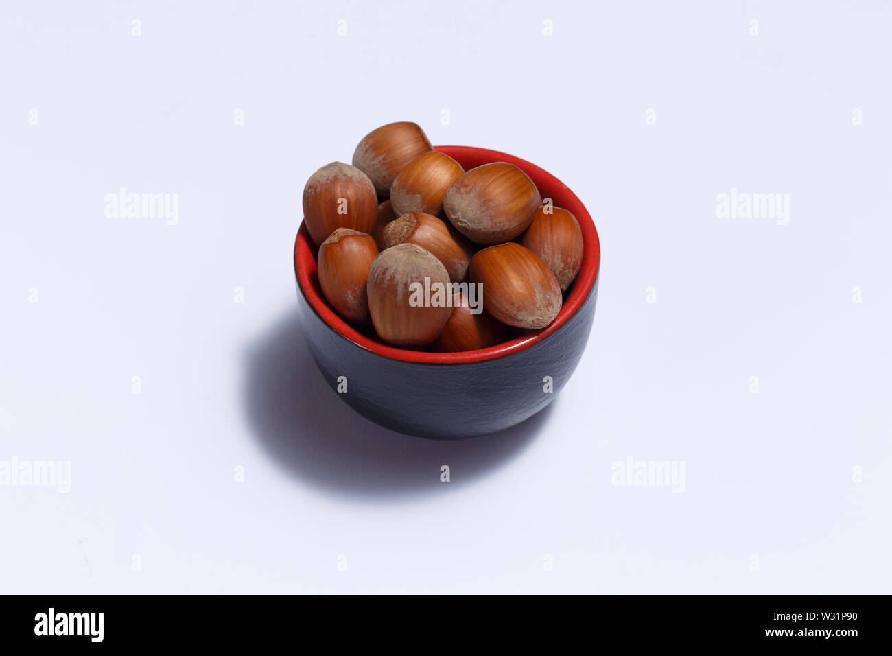 Front view of hazelnuts inside a red bowl isolated on white background ...