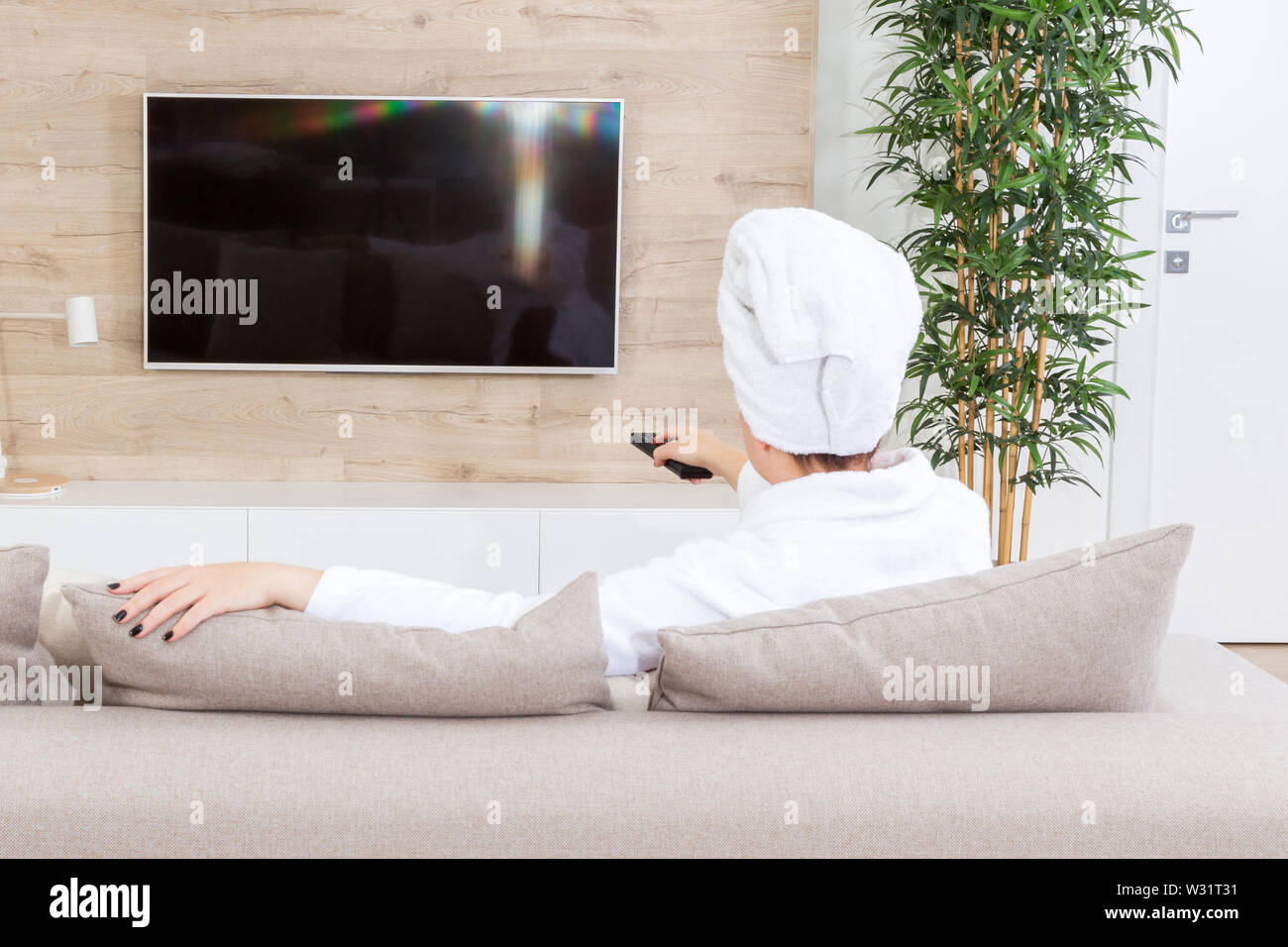 Woman with remote control sitting on couch with towel on her head ...