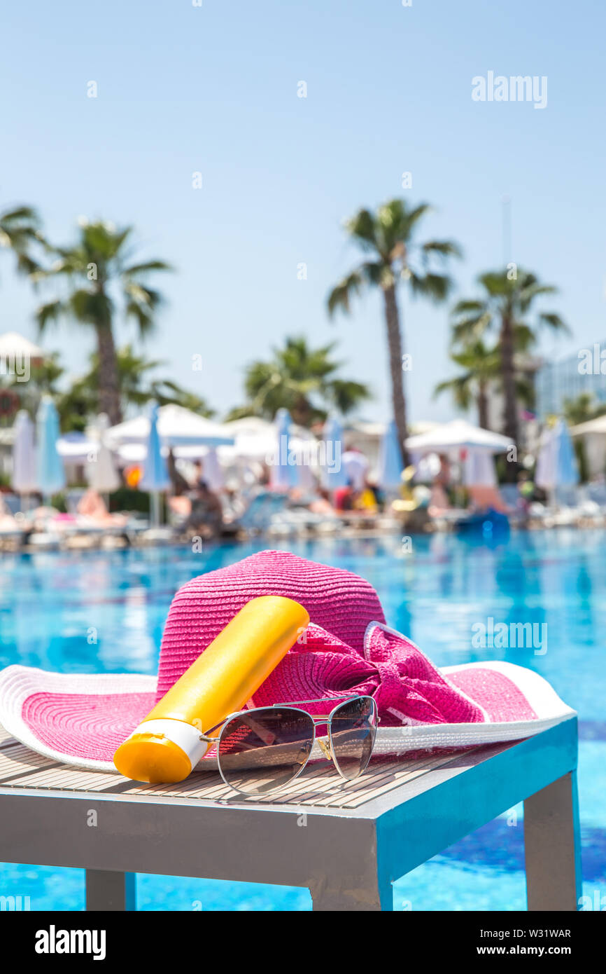 Bottle of sunscreen, hat and sunglasses next to swimming pool in hotel ...