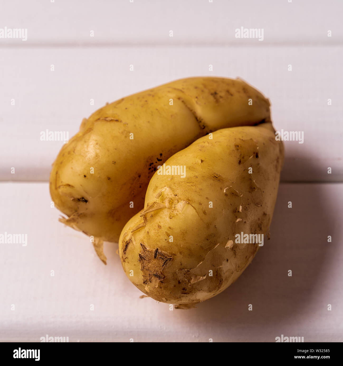 Flat lay closeup ugly curved potato on white wooden background Stock ...