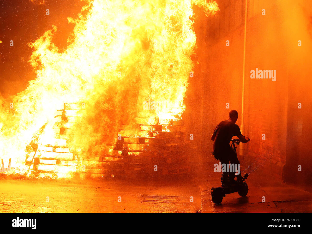 A man drives a motorised scooter past an 11th night Bonfire in Cluan ...