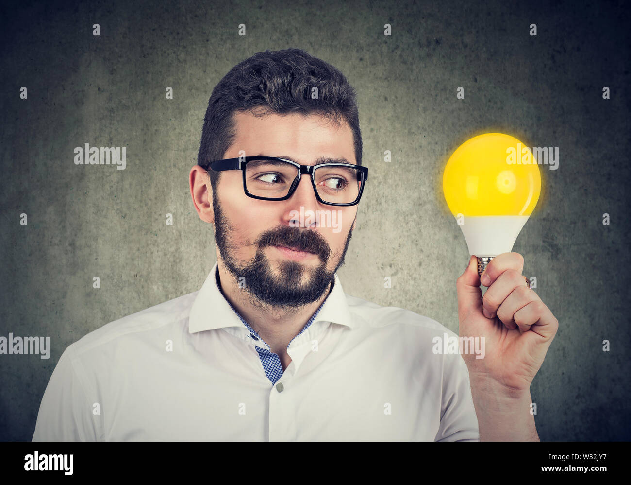 Curious young man holding looking at bright light bulb Stock Photo - Alamy