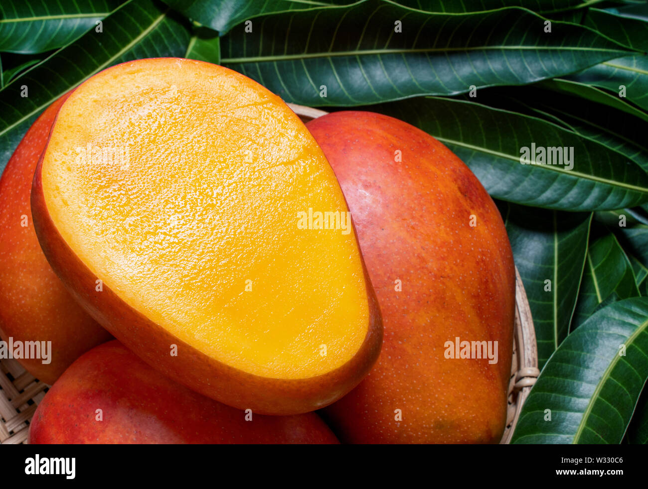 Fresh Mango - Juicy diced fruit in bamboo sieve on green color leaves ...