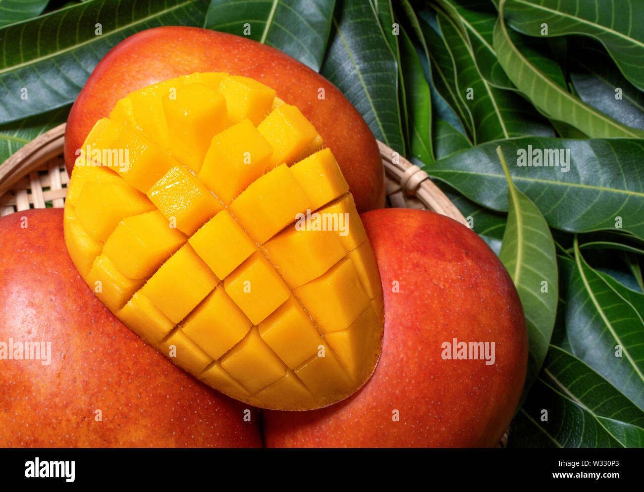 Fresh Mango - Juicy diced fruit in bamboo sieve on green color leaves ...