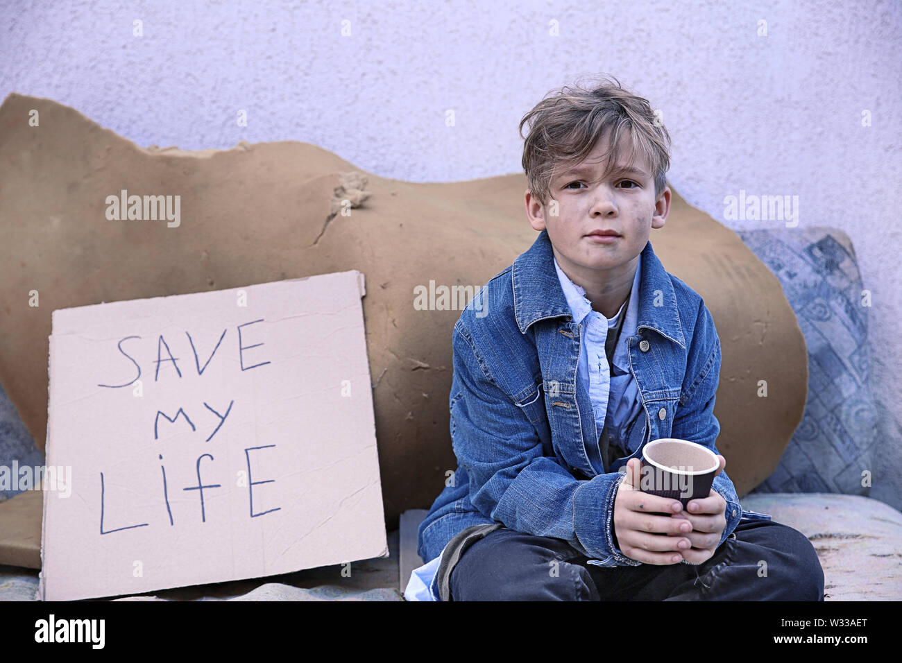 Homeless little boy with cup sitting outdoors Stock Photo - Alamy