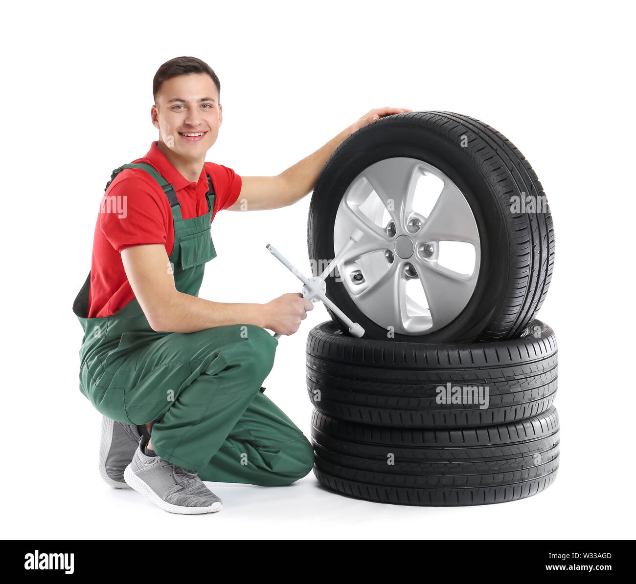 Young male mechanic in uniform with car tires and cross wrench on white ...