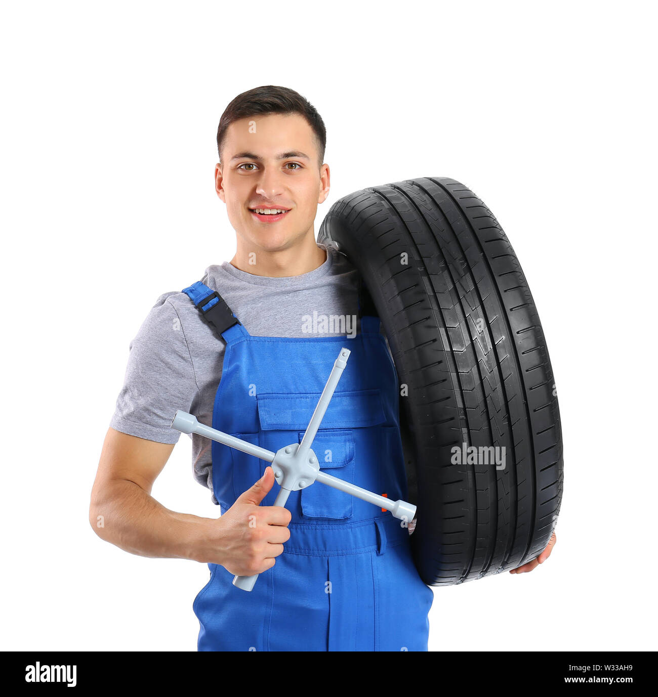 Young male mechanic in uniform with car tire and cross wrench on white ...