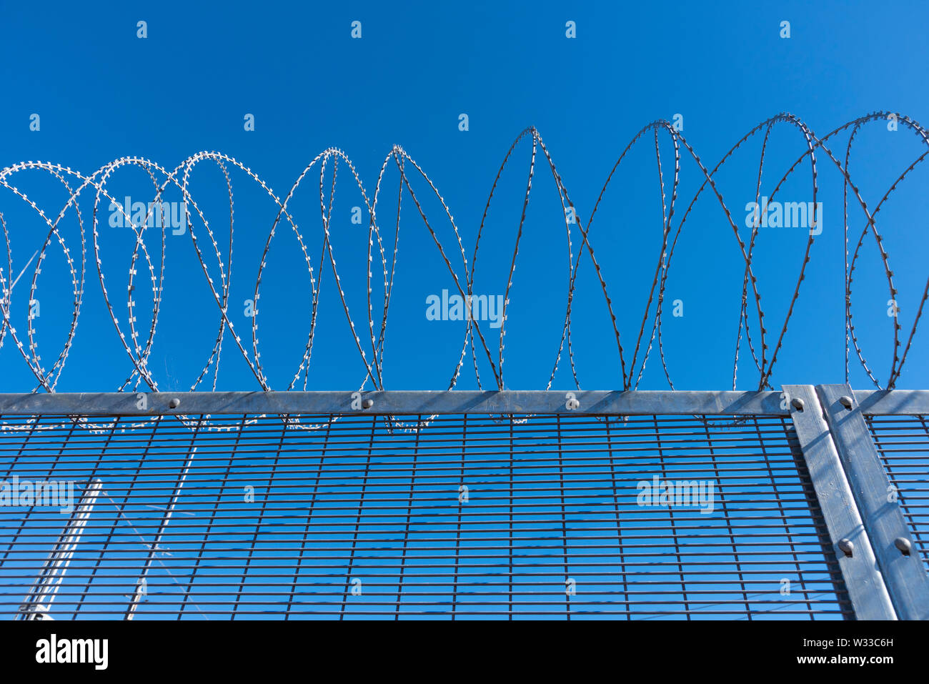 razor wire atop a security fence with deep blue sky behind Stock Photo ...