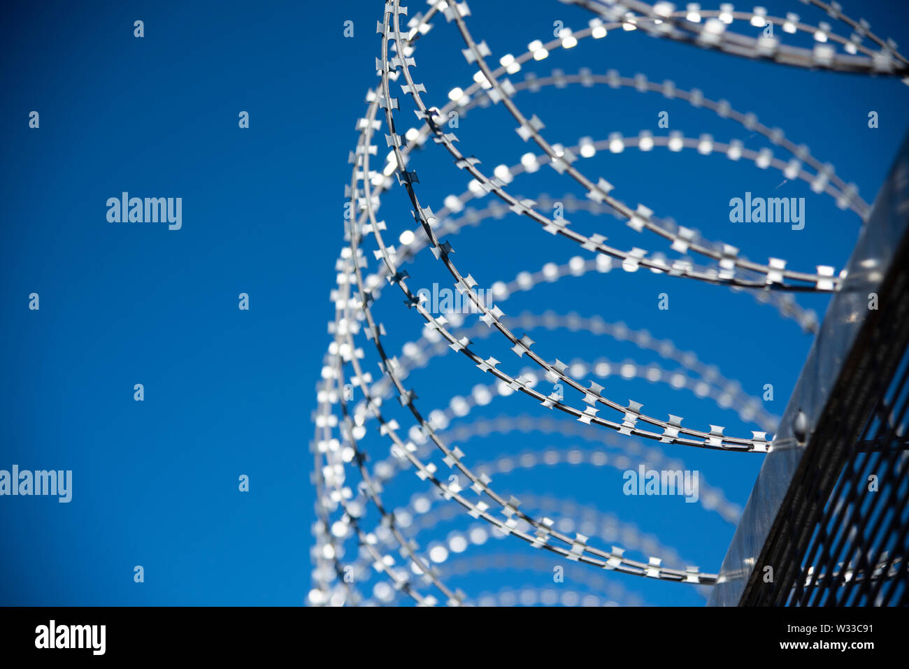 razor wire atop a security fence with deep blue sky behind Stock Photo ...