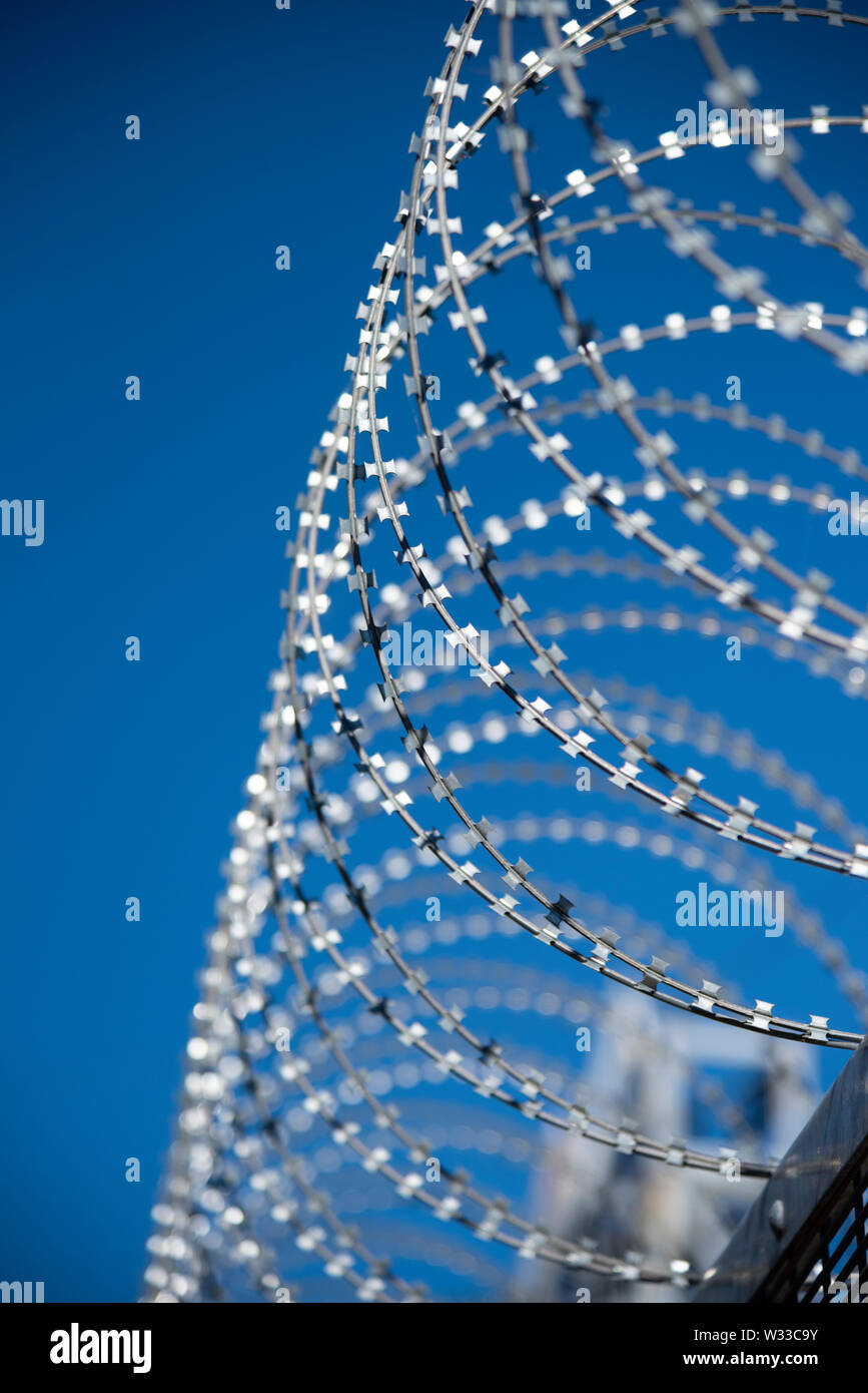razor wire atop a security fence with deep blue sky behind Stock Photo ...