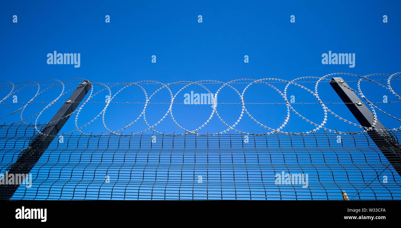 razor wire atop a security fence with deep blue sky behind Stock Photo ...