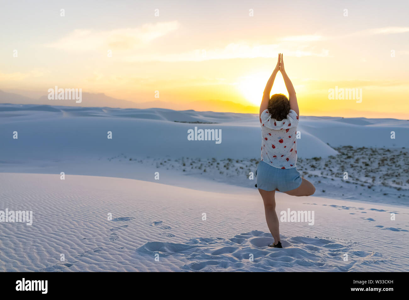 Girl woman back exercising standing balancing on one leg in white sands ...
