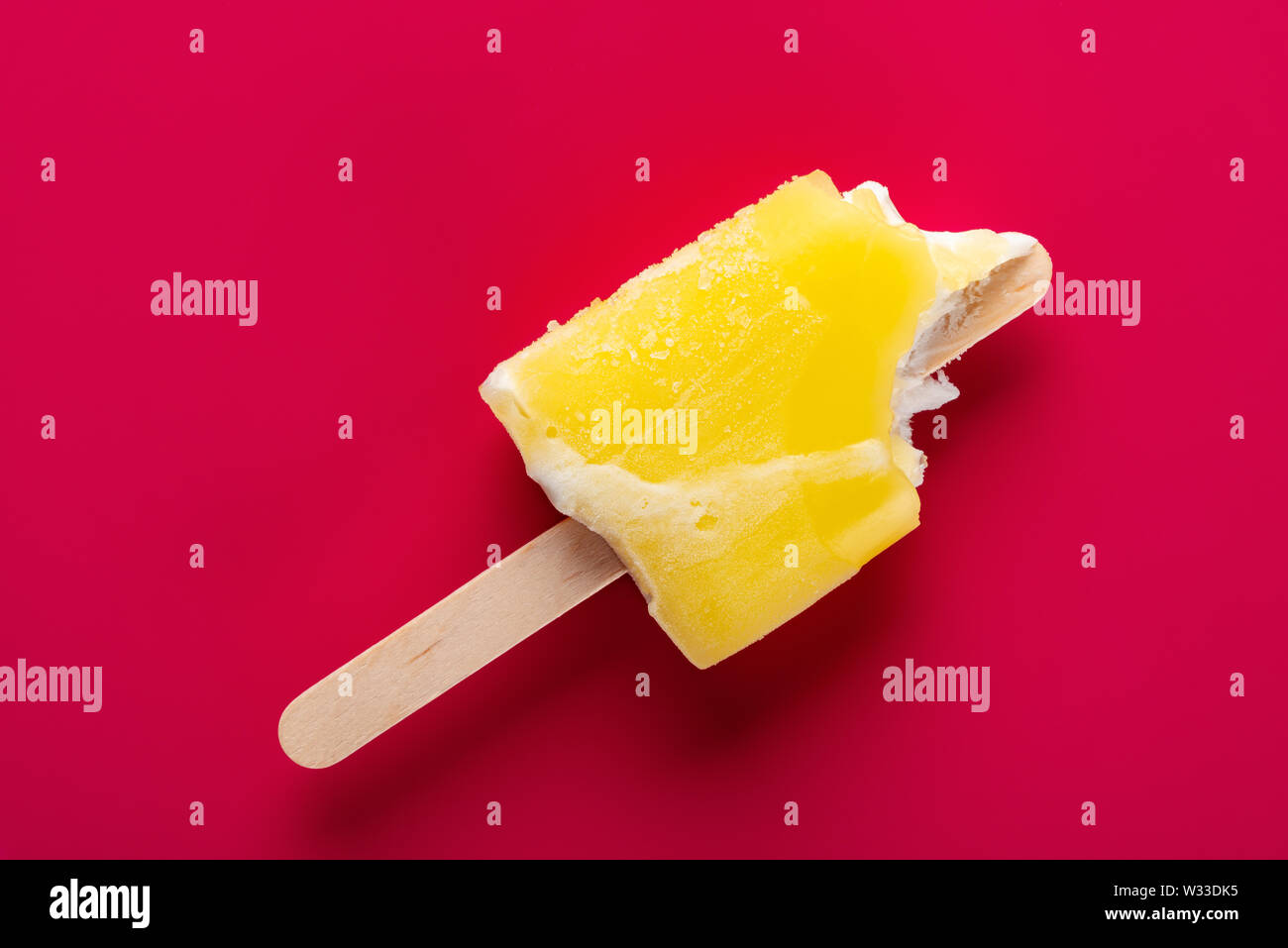 yellow popsicle with a couple of bites on a red background Stock Photo ...