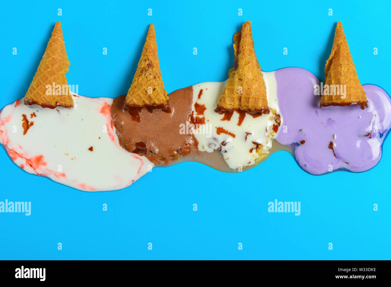 top view multiple flavor ice cream cones melted on blue background ...