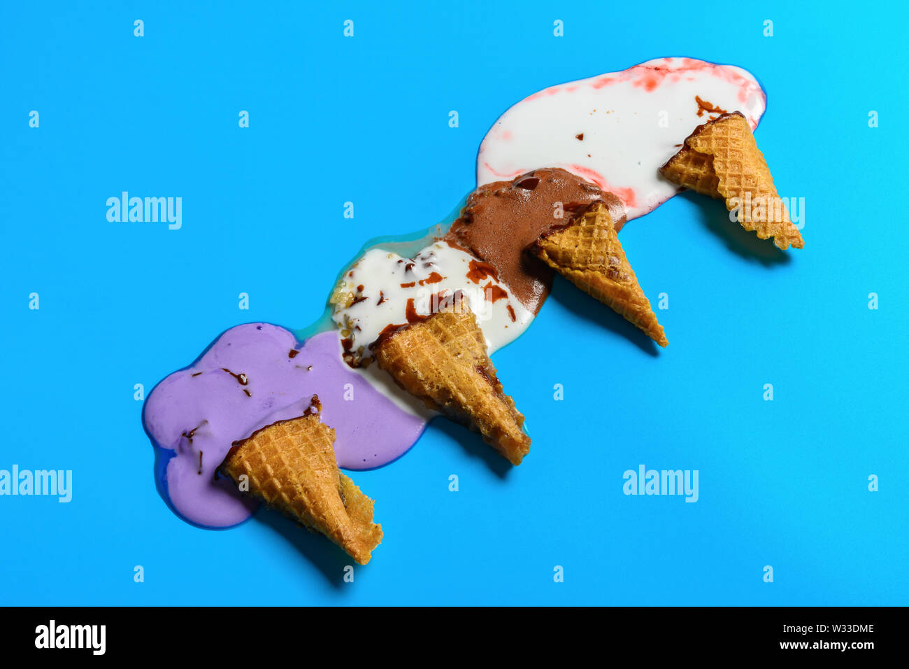angle view multiple flavor ice cream cones melted on blue background ...