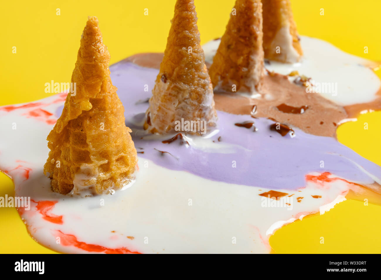 side view multiple flavor ice cream cones melted on yellow background ...