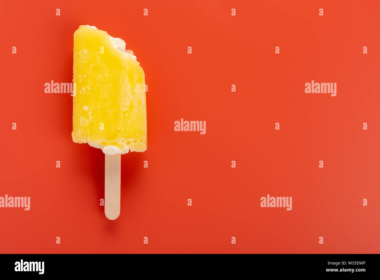 yellow popsicle with a couple of bites on an orange background Stock ...