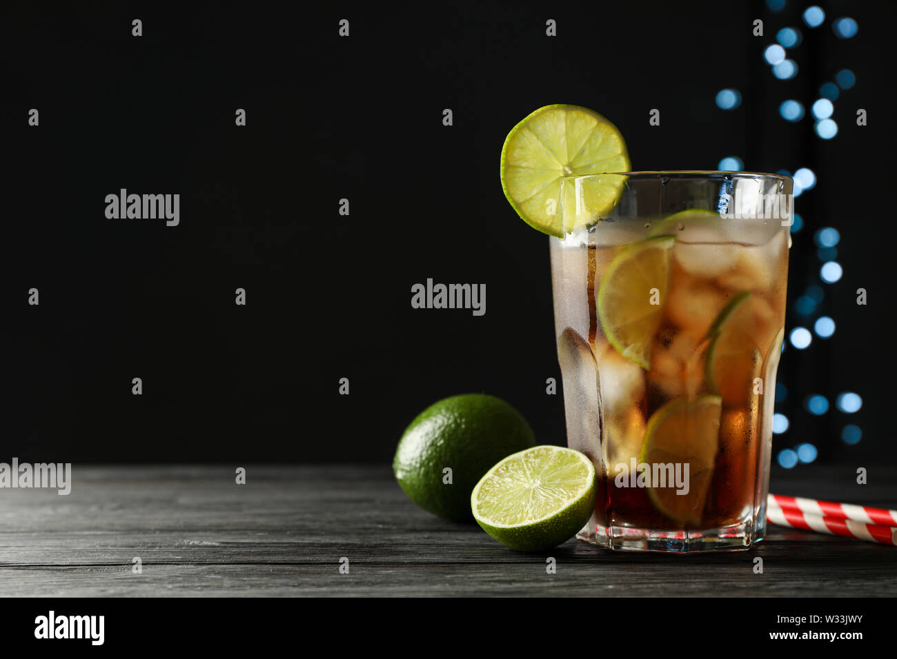 Glass of cold cola with citrus and ice on wooden table against dark ...
