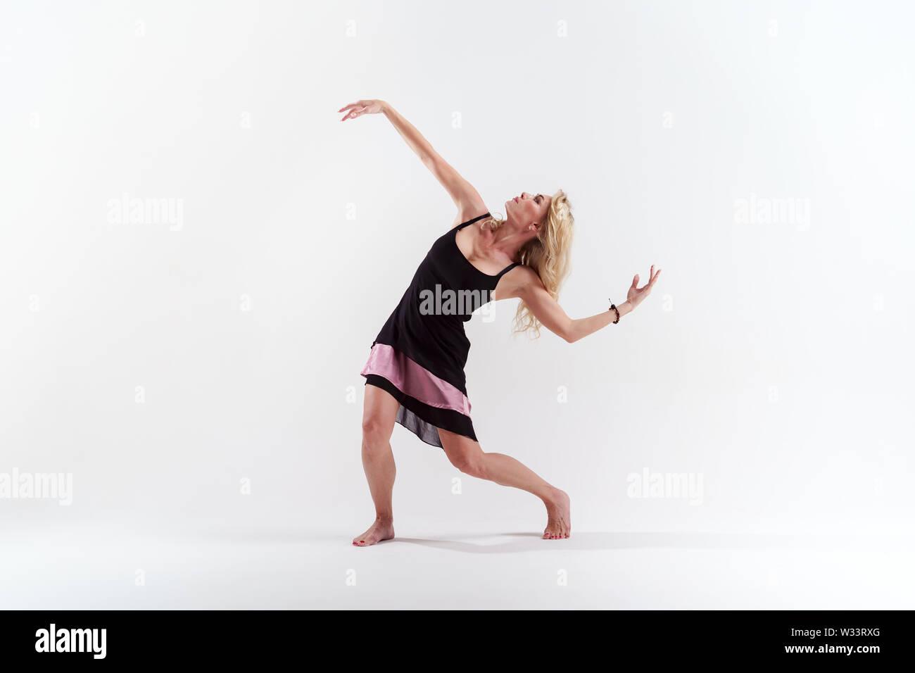 Beautiful blonde woman looking up dancing in studio on blank white ...