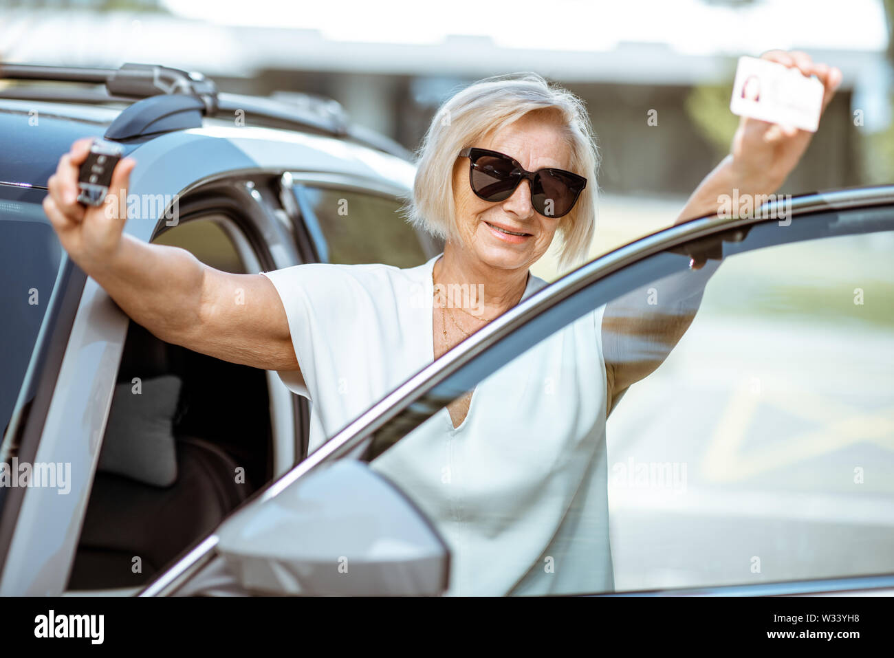 Portrait of a happy senior woman showing driver's license and keys ...