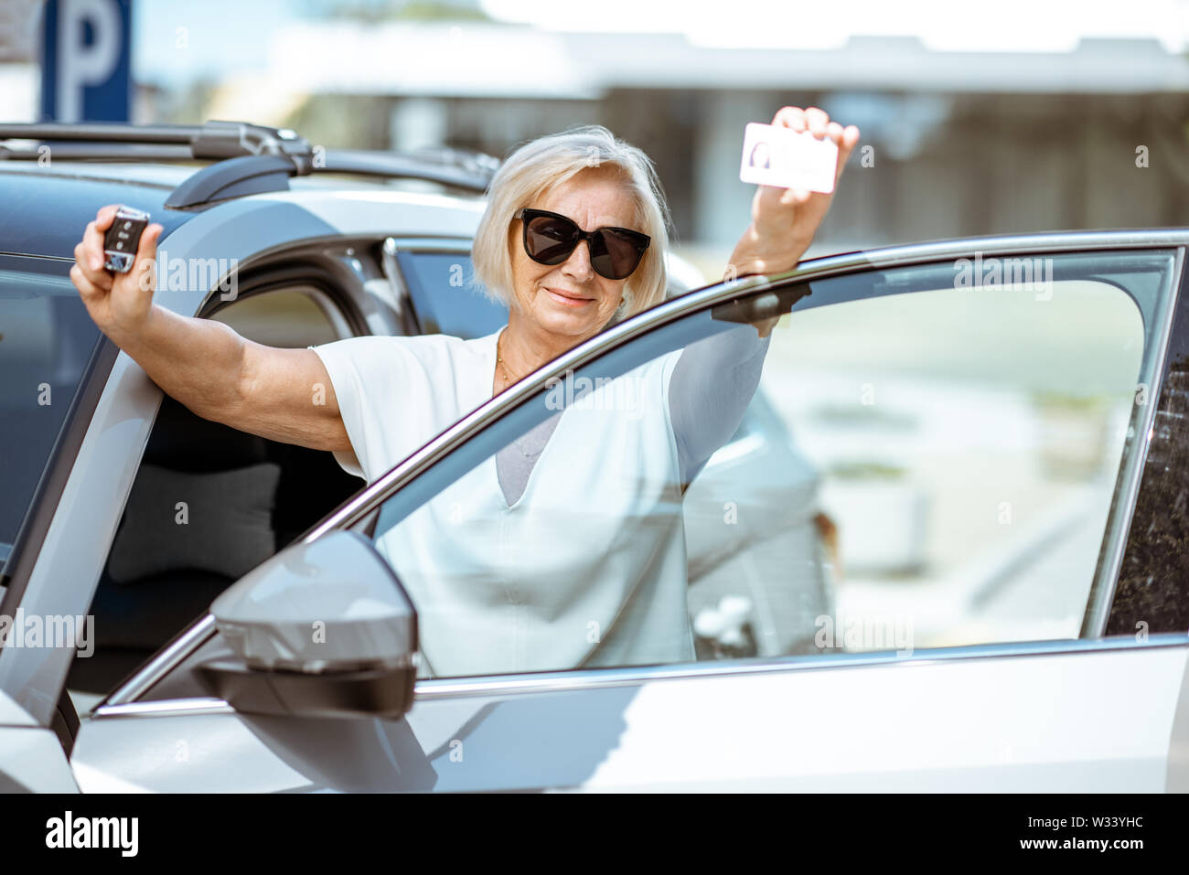 Portrait of a happy senior woman showing driver's license and keys ...