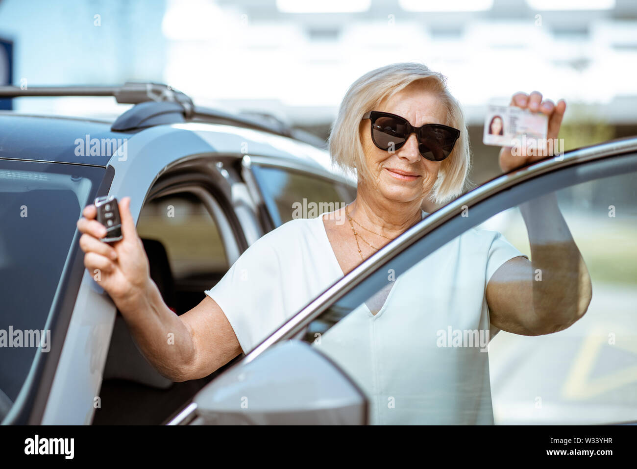 Portrait of a happy senior woman showing driver's license and keys ...