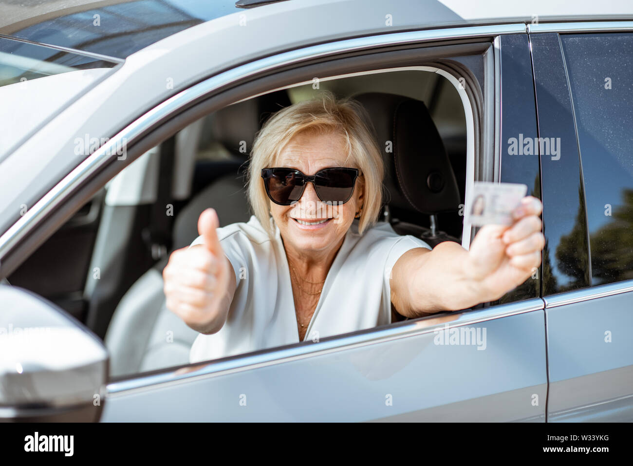 Portrait of a happy senior woman showing driver's license, while ...