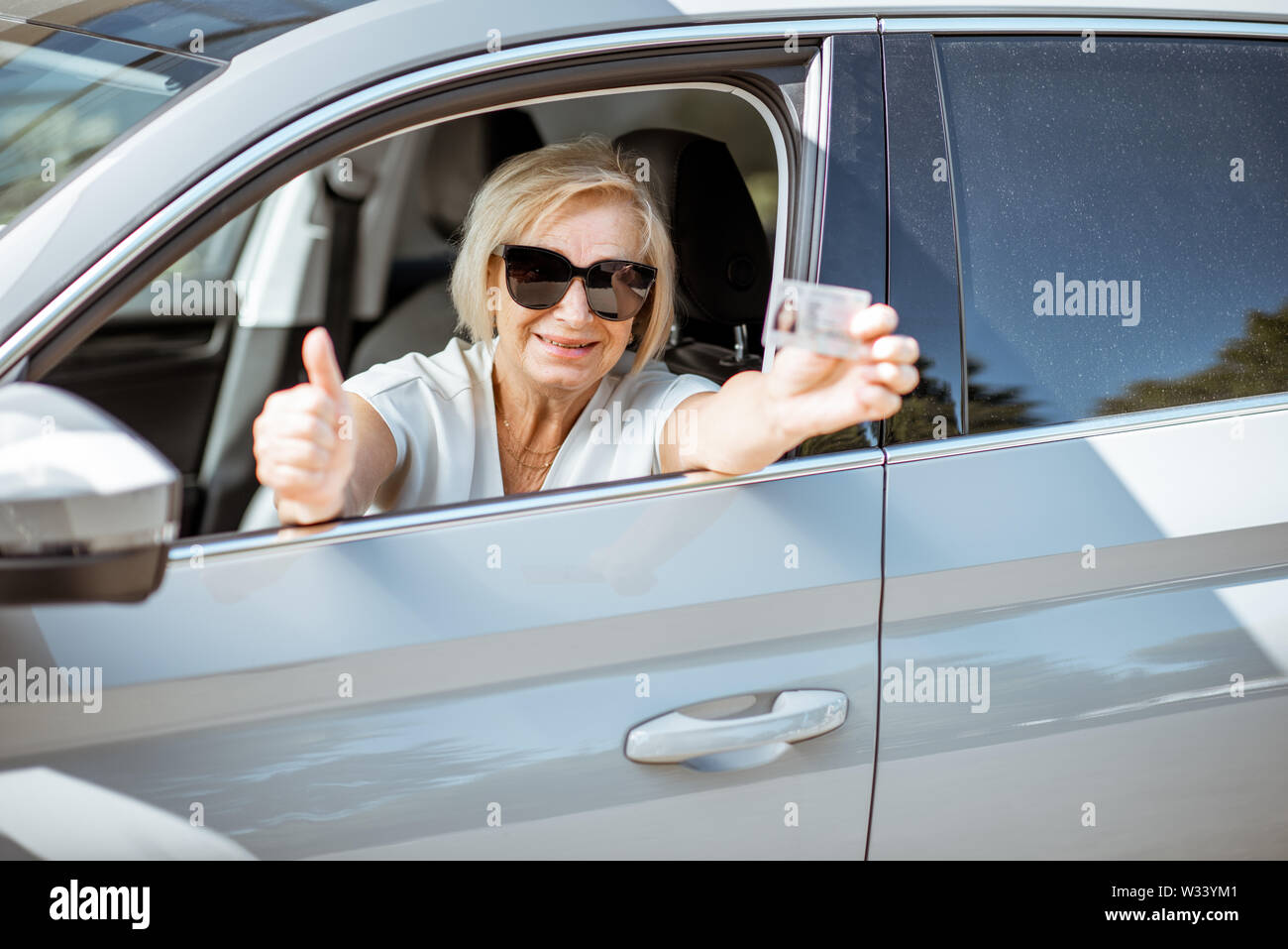 Portrait of a happy senior woman showing driver's license, while ...