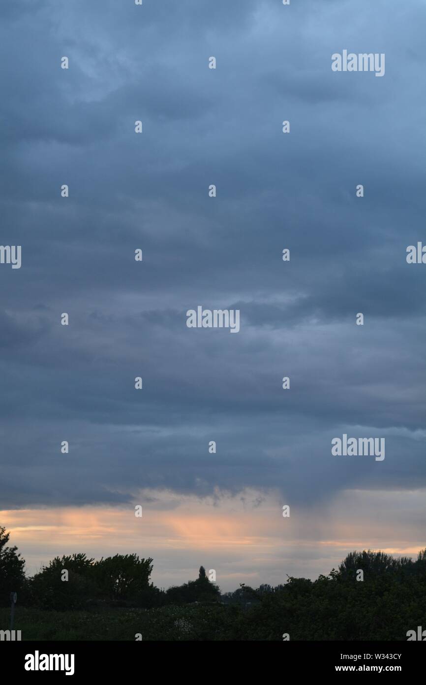Evening clouds as the sun sets against the horizon with a rain burst in ...