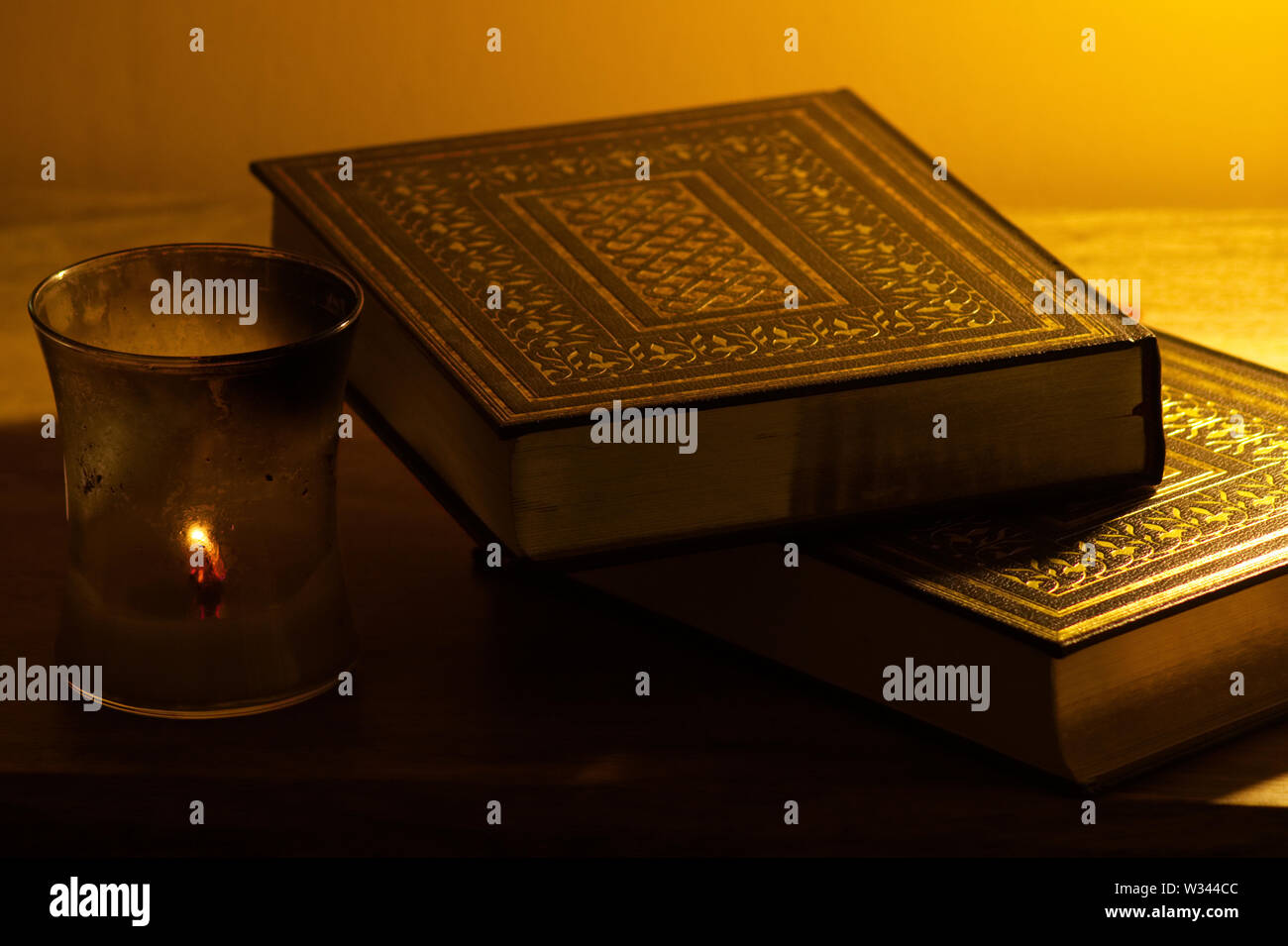 Copies of old religious books and texts next to a lit candle against a ...