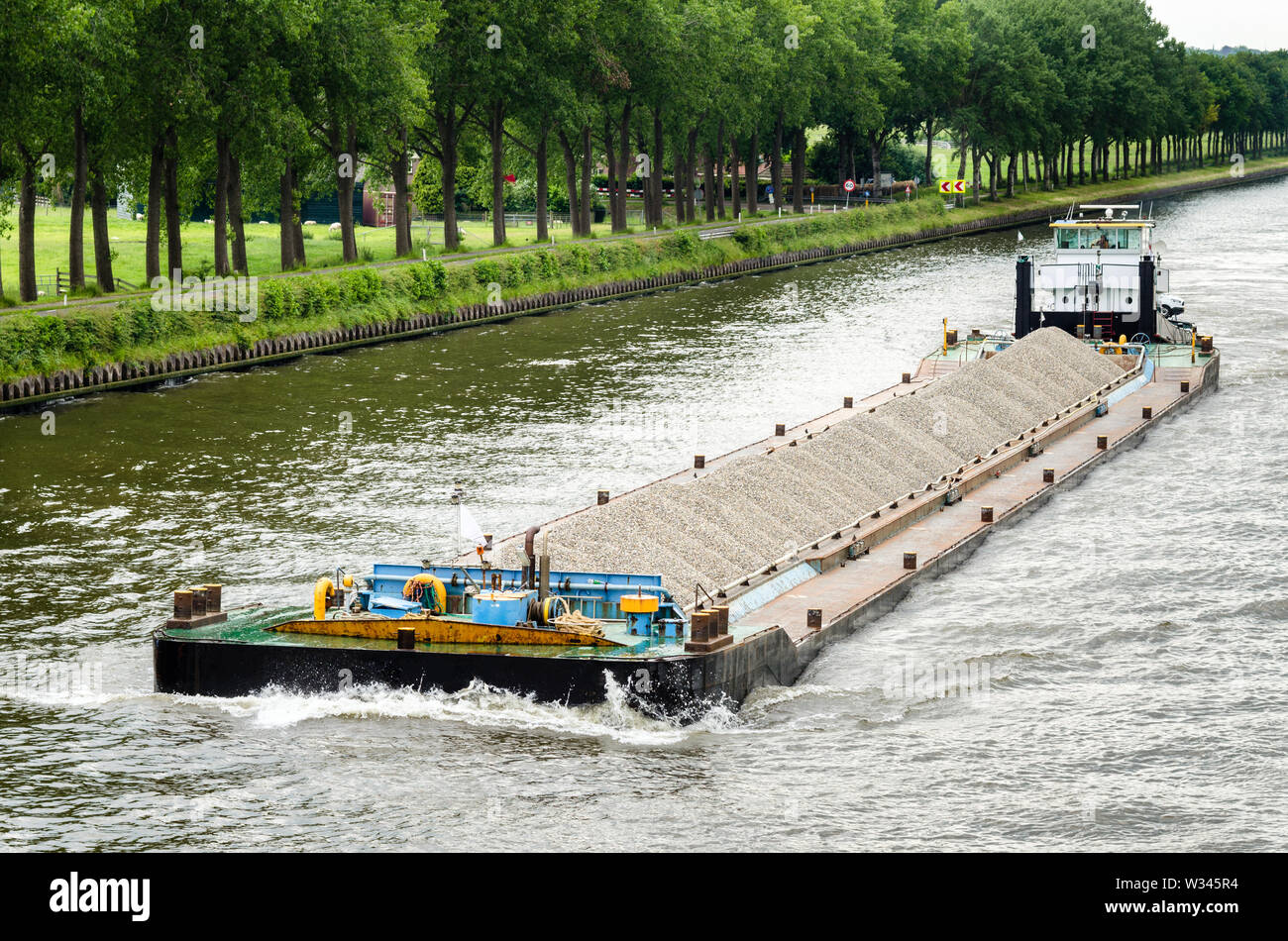 Barge loaded with Gravel Sailing up a tree lined canal in the ...